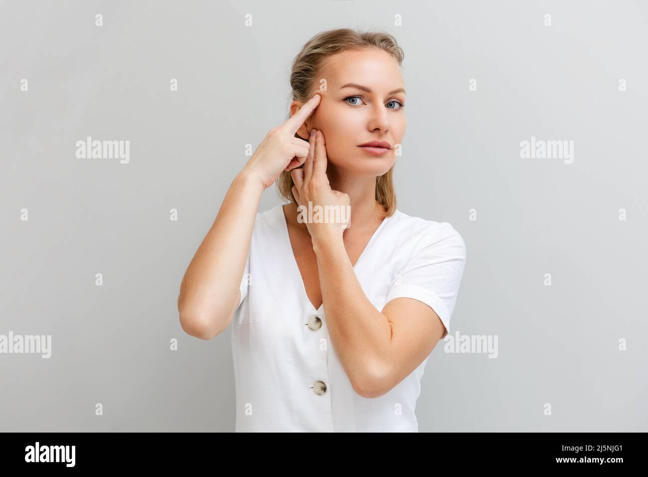 Portrait of a young beautiful woman, pulling the skin on her temples ...