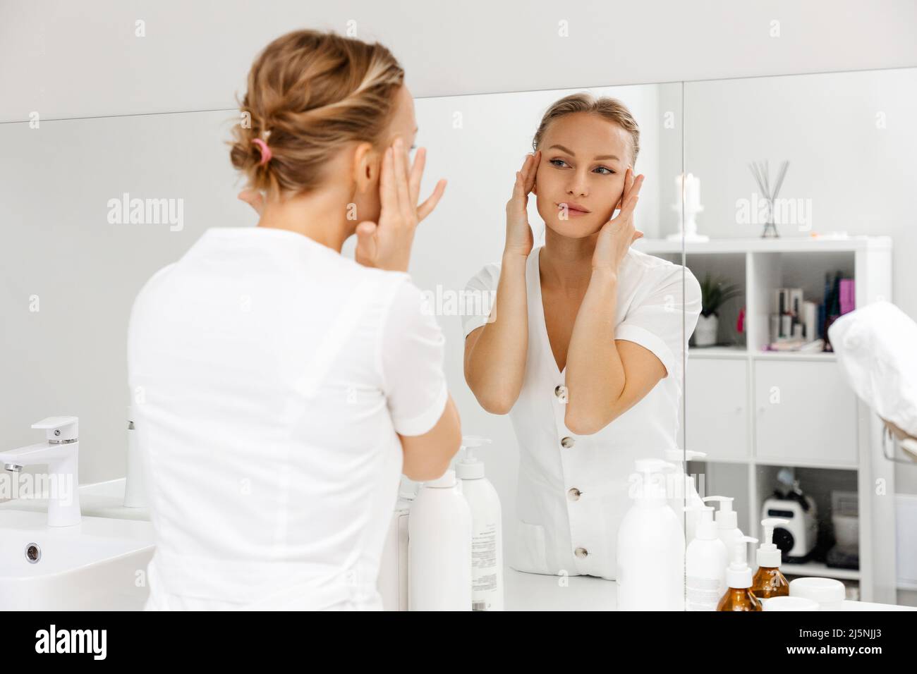 A young beautiful woman looks in the mirror and pulls the skin on her ...