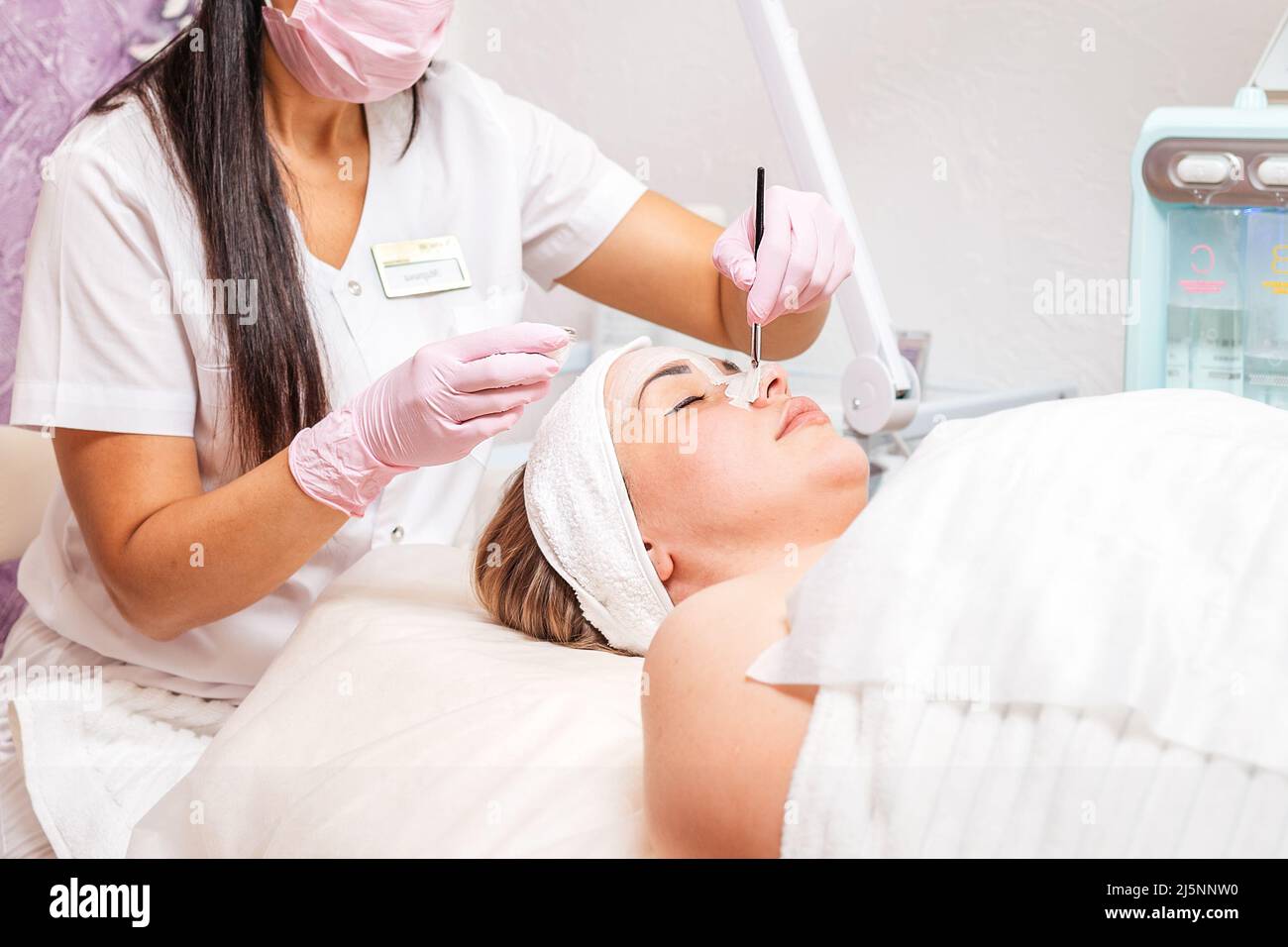A cosmetologist in a medical mask and gloves holds a bowl of cosmetics ...
