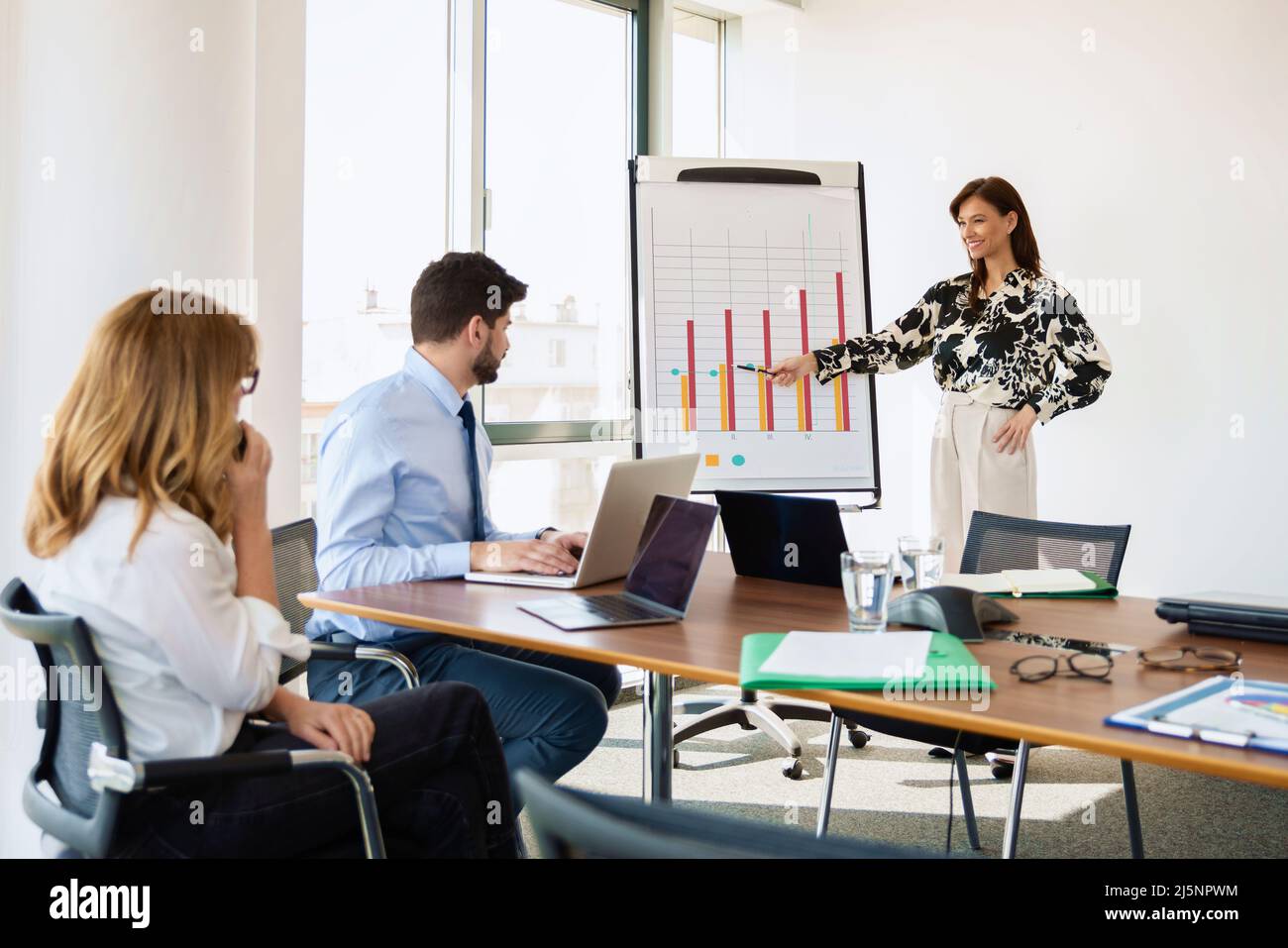 Businesswoman pointing at a chart on a whiteboard during business meeting. Group of business ...