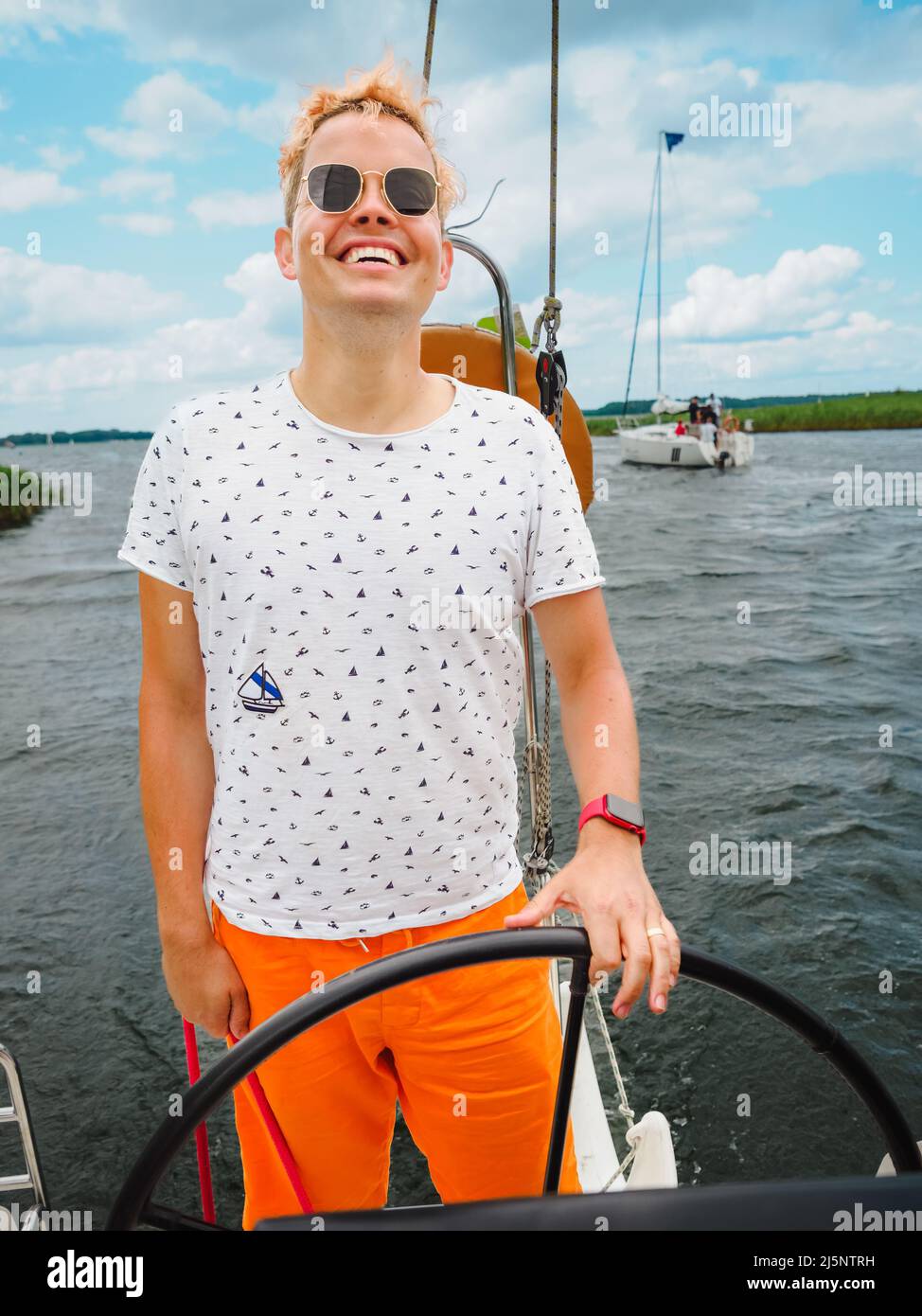 handsome smiling blond hair young man steering wheel a sailboat or ...