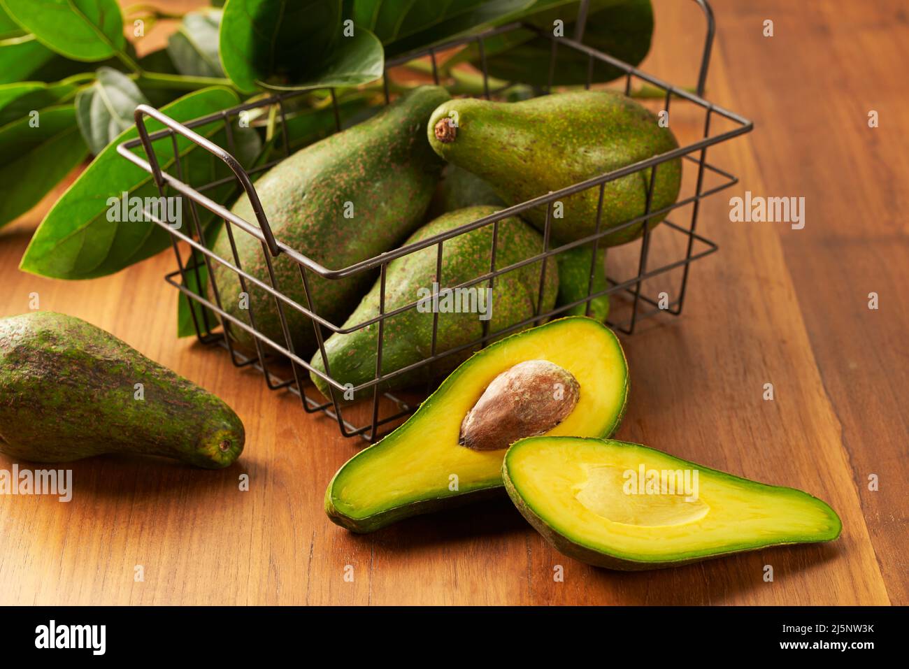 A collection of avocados in an iron basket with one fruit split in the ...