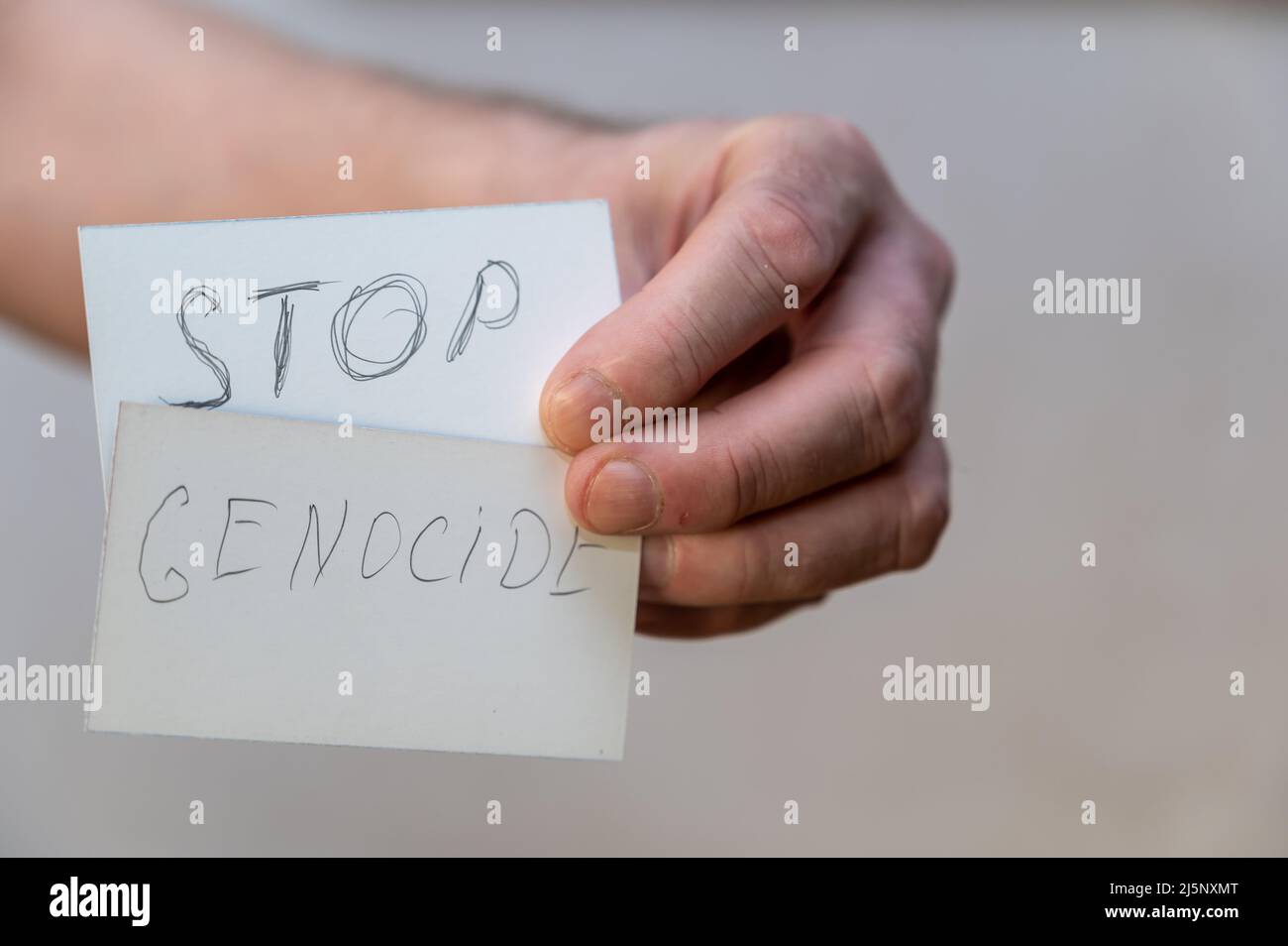Stop Genocide. Words written in jagged letters. A man's hand holds two ...