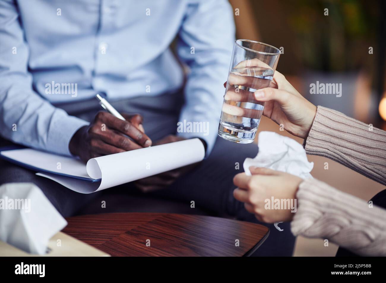Hands of woman crying and drinking water during therapy session with ...