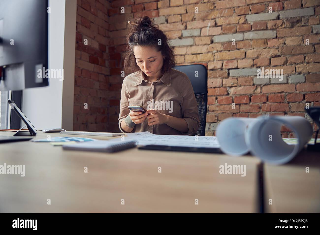 Female interior designer using smartphone while working in her office ...