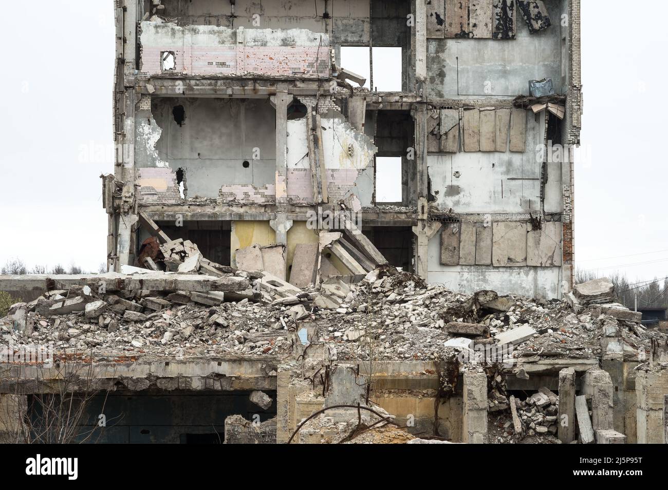 A ruined building against a gray sky with piles of concrete rubble and ...
