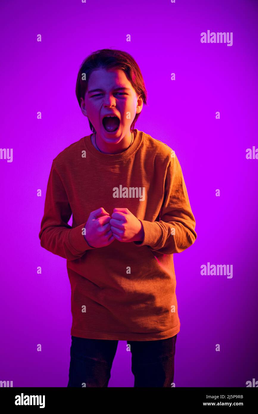 Portrait of emotive boy, child shouting, screaming isolated over purple ...