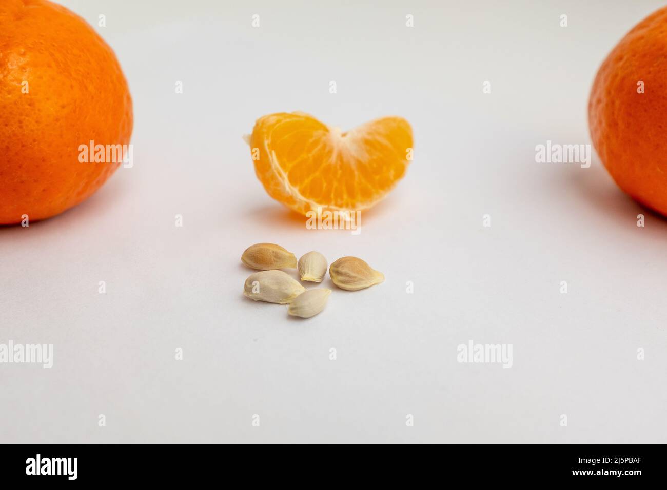 Two orange and one slice with five seeds on a white background, side ...