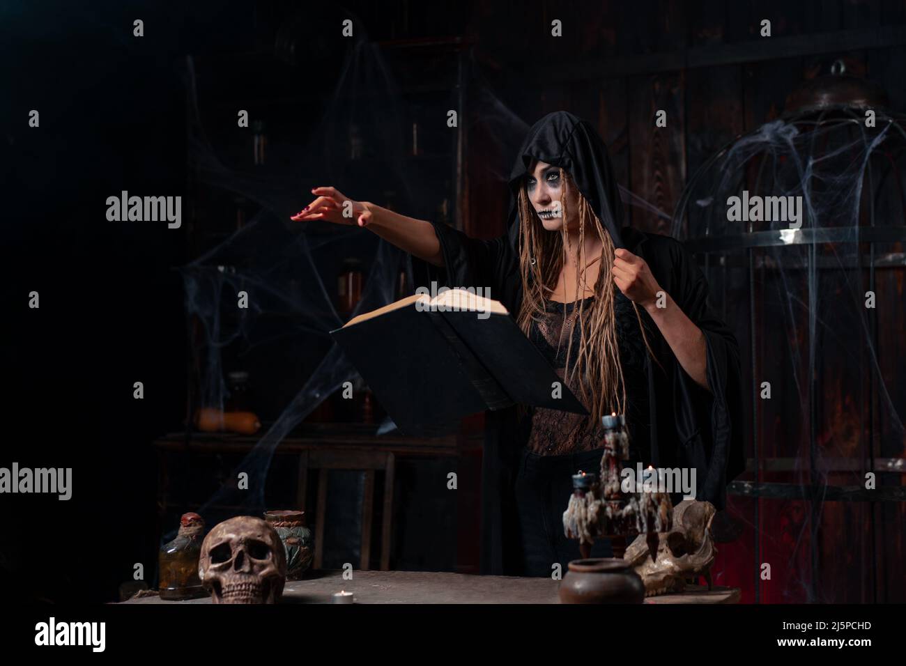 Halloween concept. Witch dressed black hood standing dark dungeon room ...