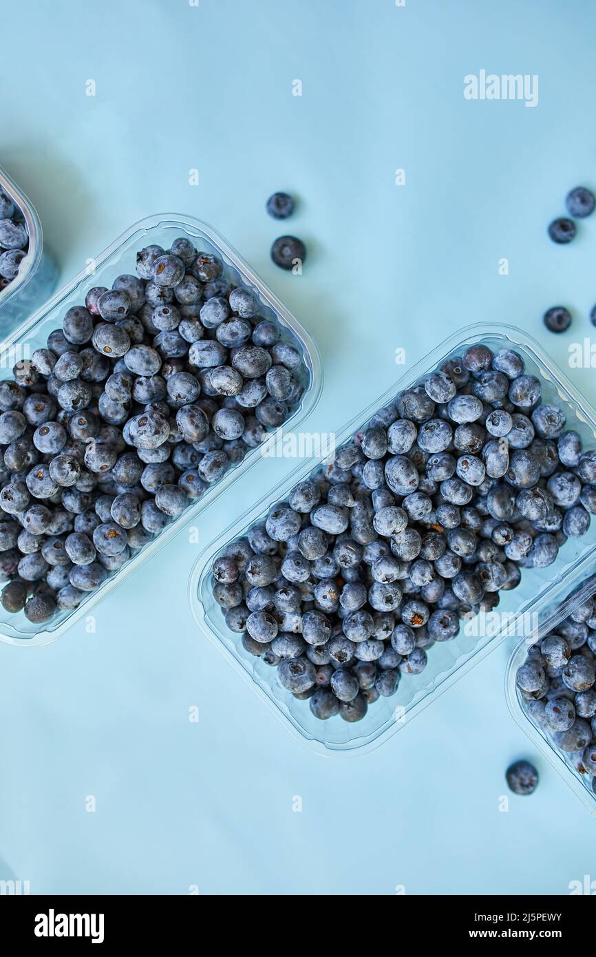 Flat lay of fresh organic juicy blueberries in a box on blue background ...