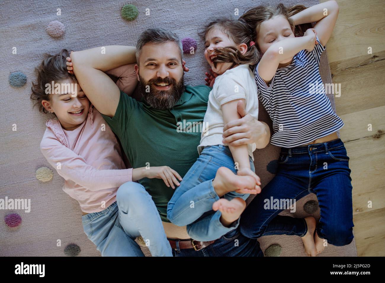 Top view of cheerful father with three little daughters lying on floor ...
