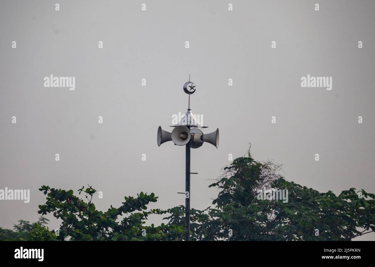 A mosque loudspeaker on a pole on the roof plays the call to prayer ...