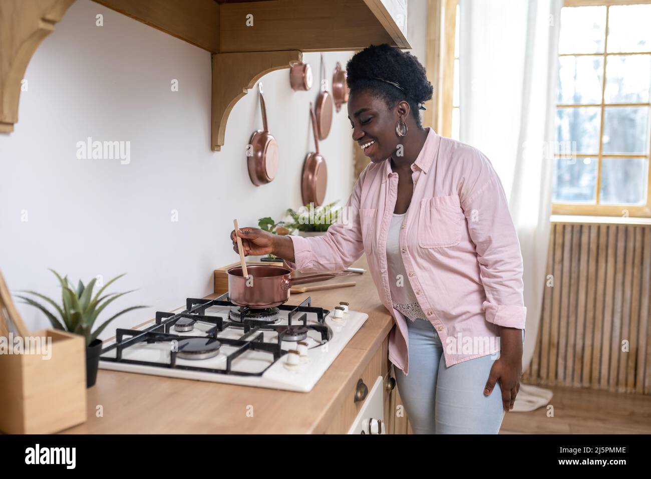 Contented african woman in pink clothes cooking in the kitchen Stock ...