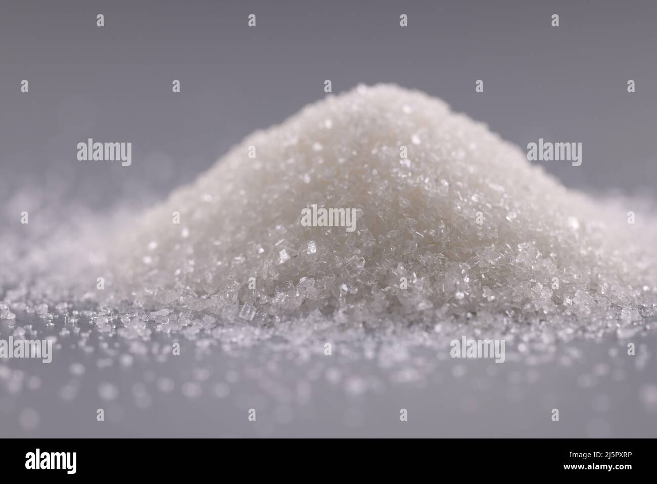 Pile of sugar crystals on grey surface, heap of sweet powder to add in ...