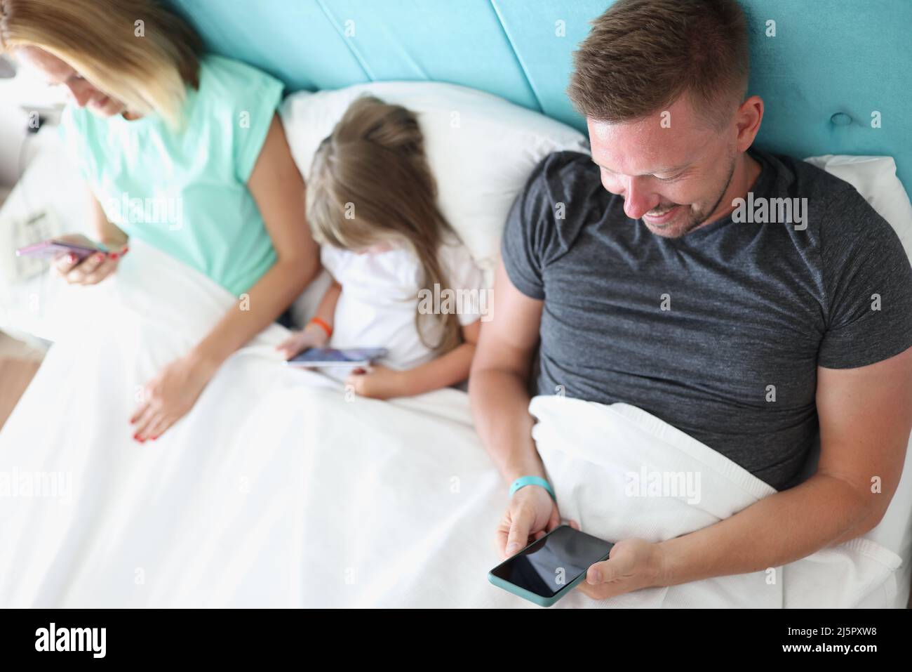 Young family with kid using gadgets while lying together in bed Stock ...