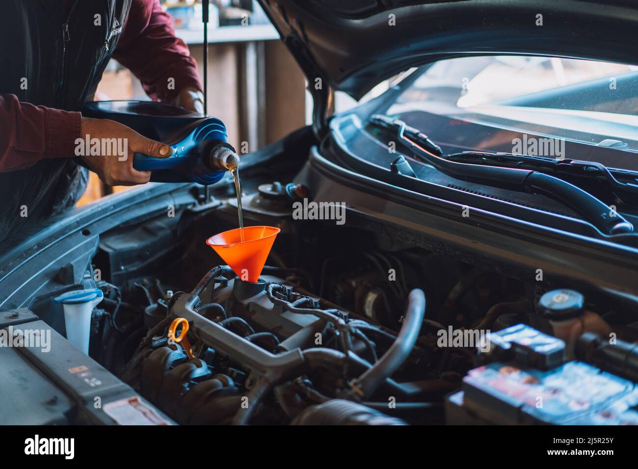 Man pours new oil into the engine through red funnel Stock Photo - Alamy