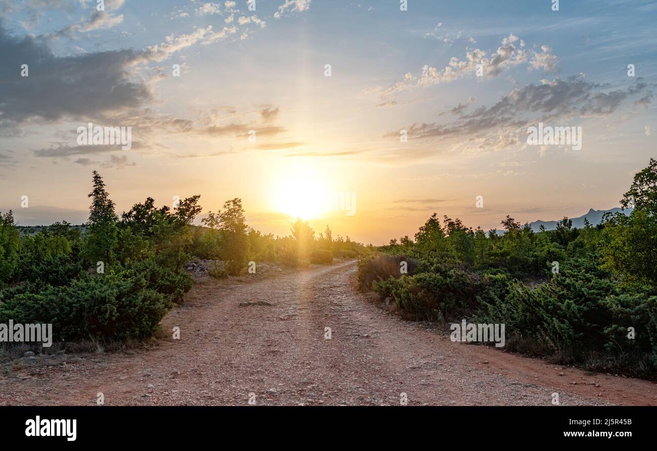 Picturesque dirt road against the backdrop of sunset and mountains ...