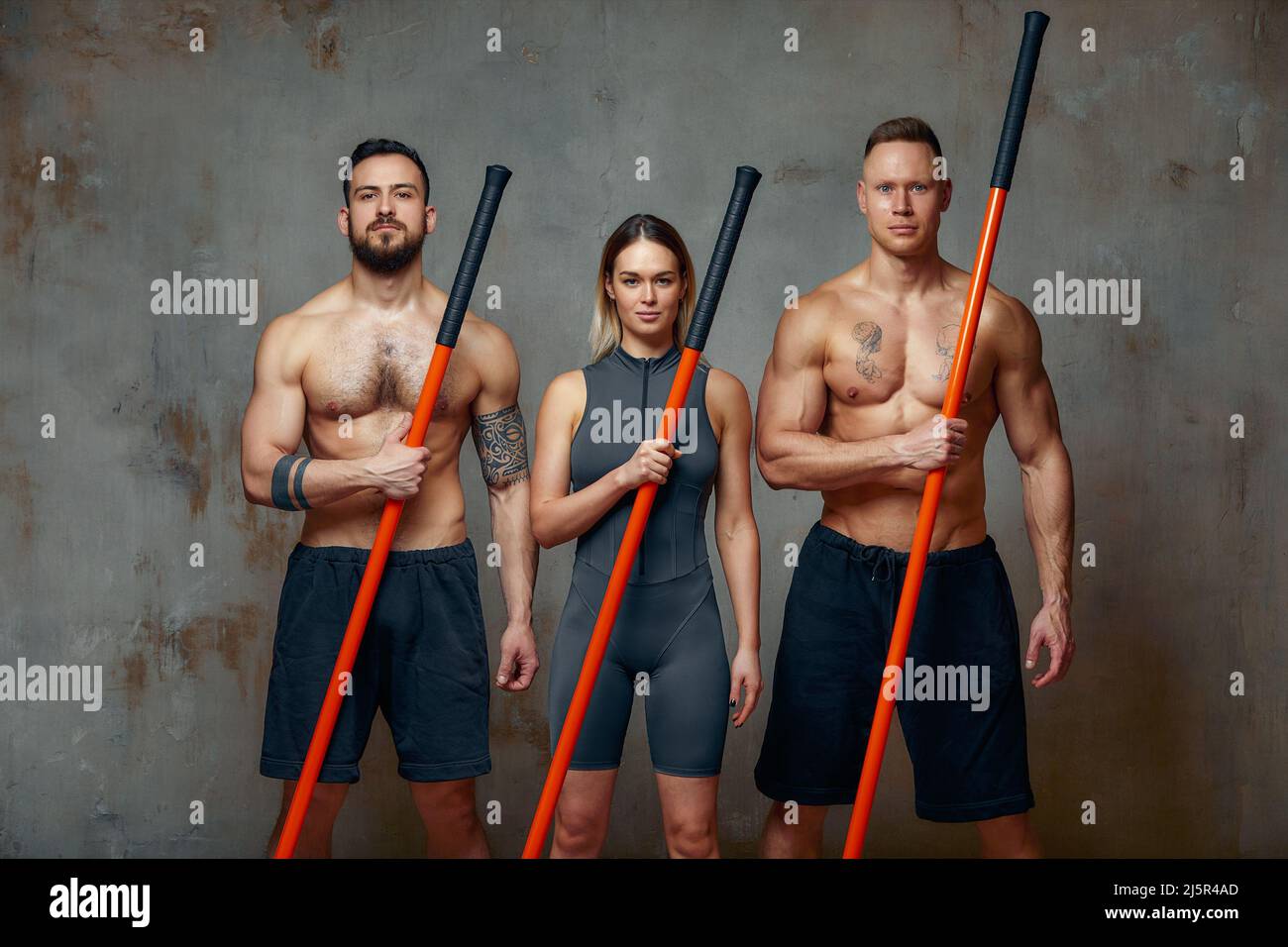 Two men and woman aikido fighters with wooden fight stick posing in ...