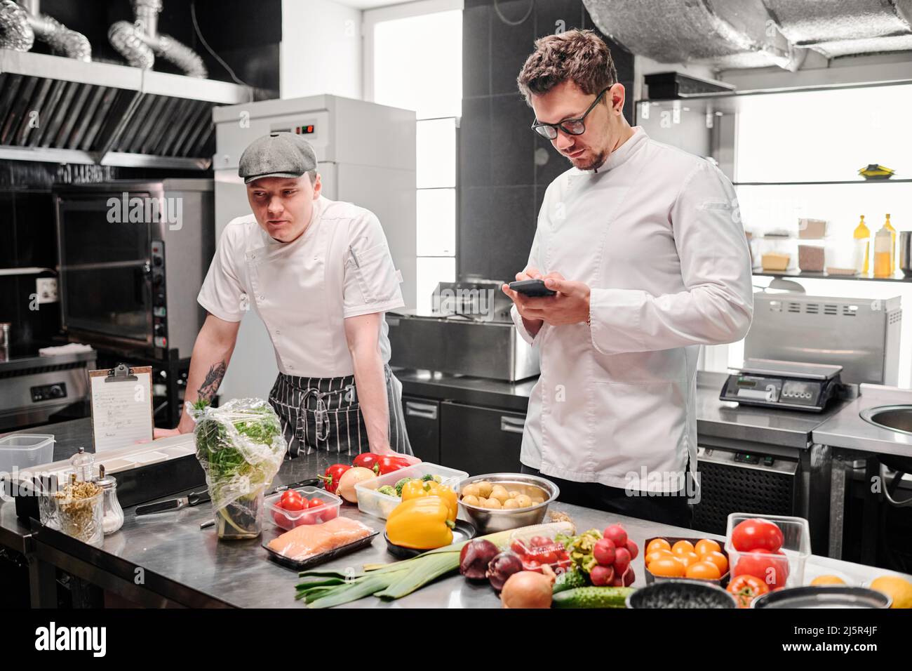 Young chef in uniform using his mobile phone to check list of fresh ...