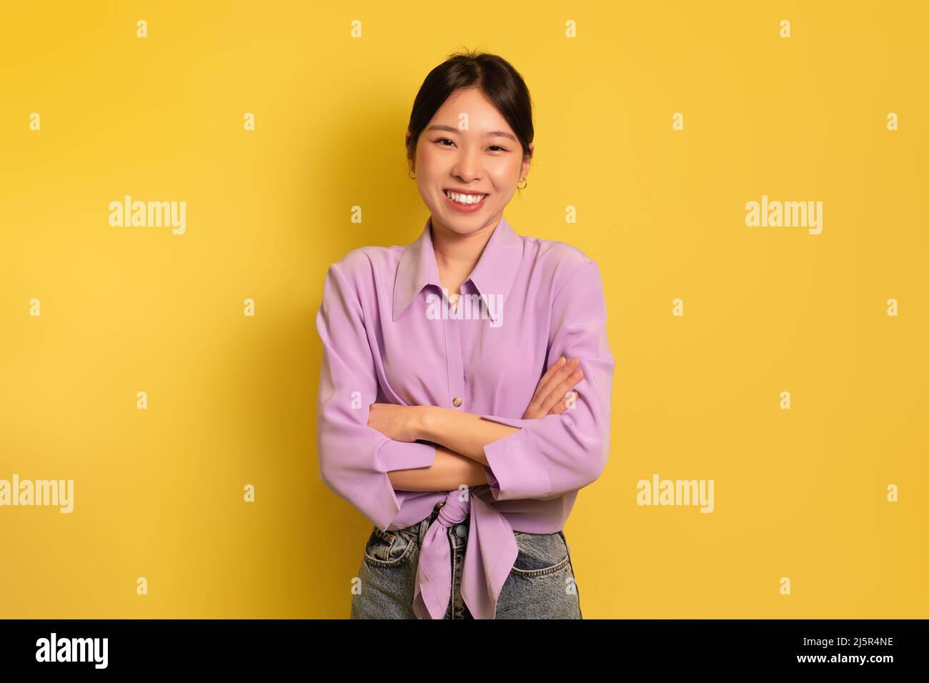 Positive young Asian woman standing with crossed arms and looking to ...