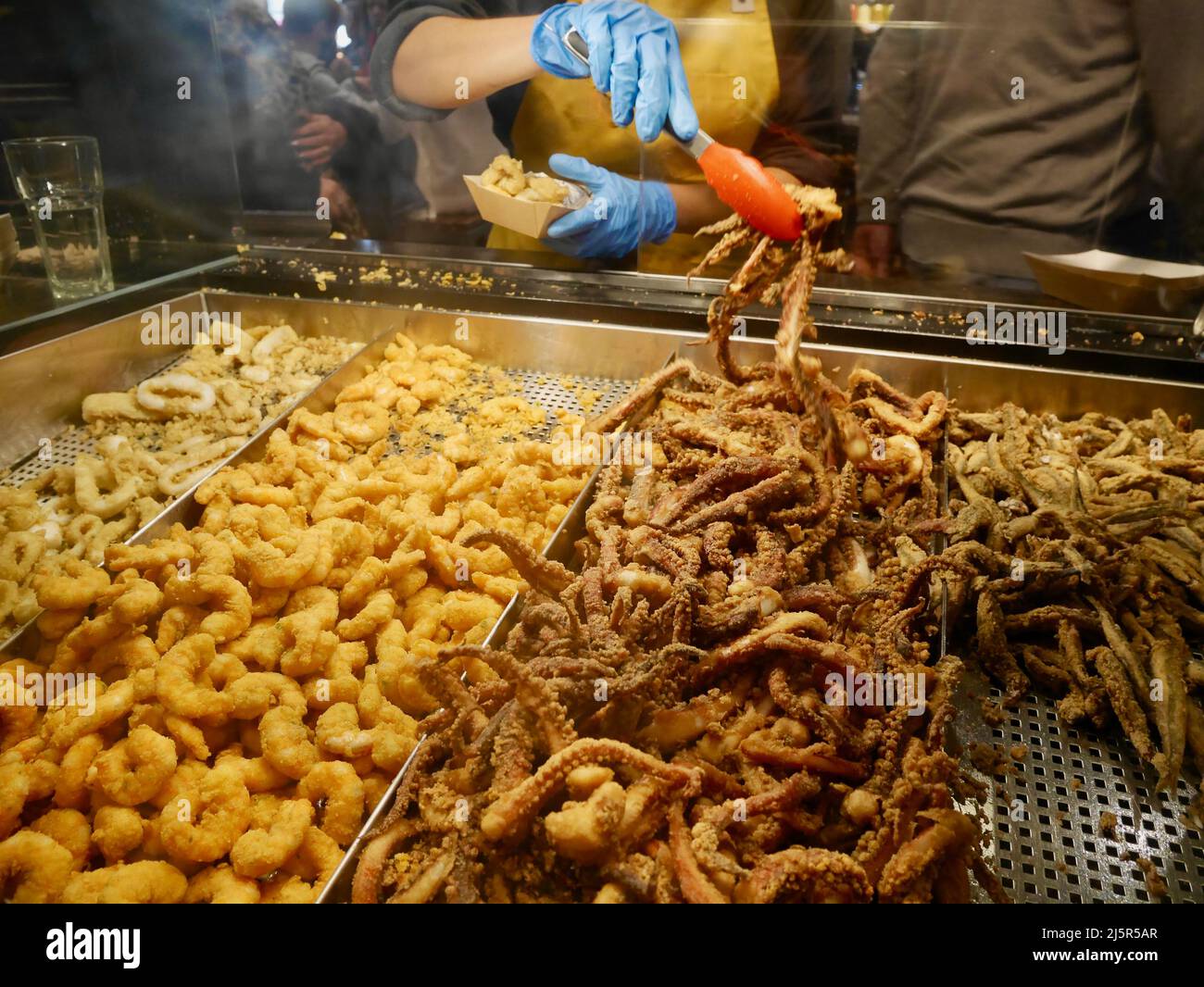 Woman behind counter at Mercado de San Miguel putting mixed fried ... Woman behind counter at Mercado de San Miguel putting mixed fried ...
