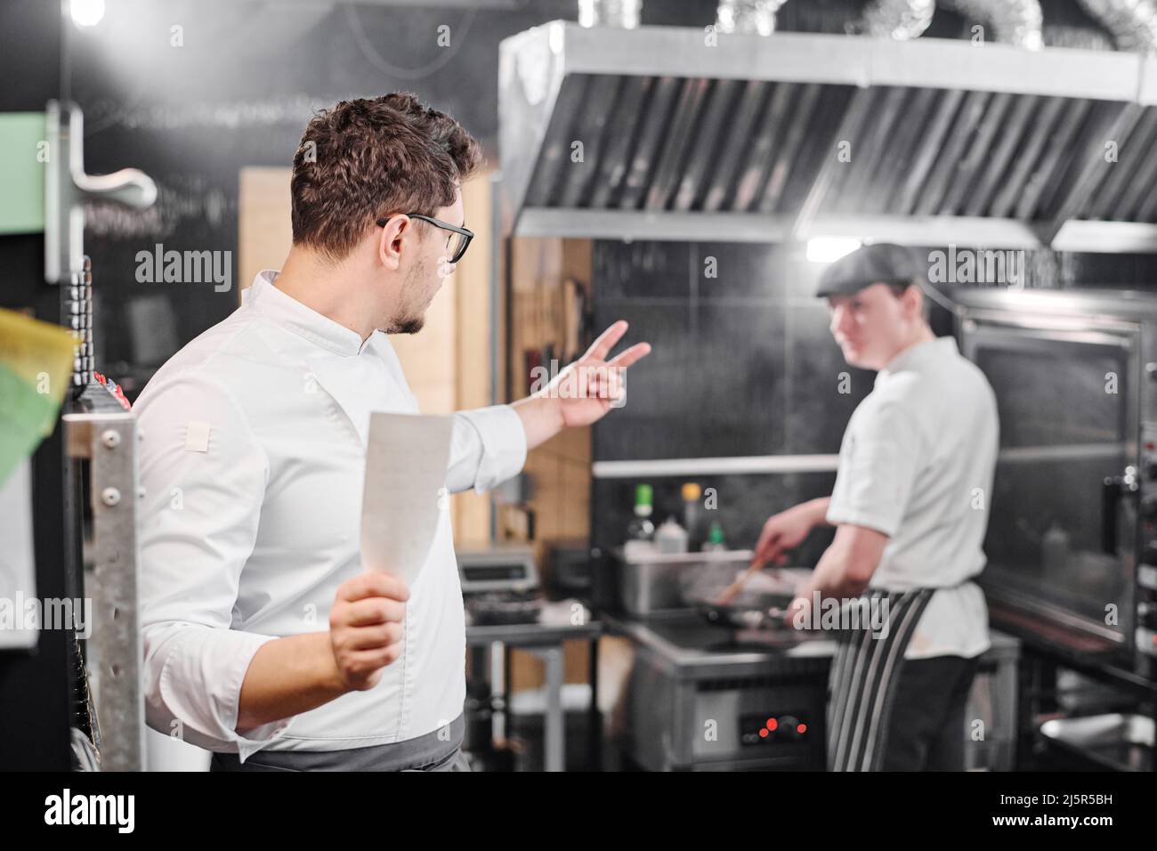 Chef gesturing his assistant to prepare food for two people during ...
