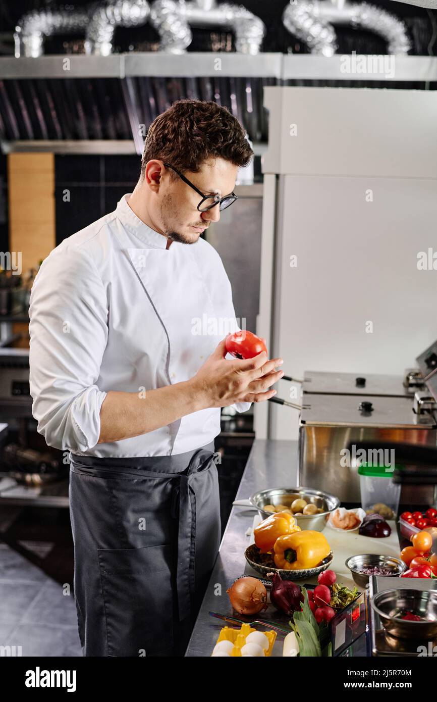 Serious chef in uniform examining products on table and choosing ...