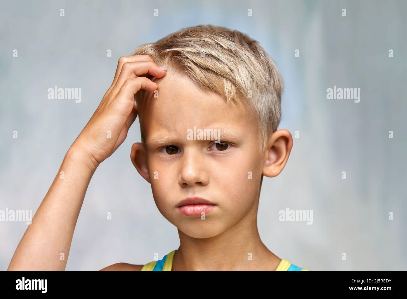 Confused junior schooler puts hand on head looking in camera. Portrait ...