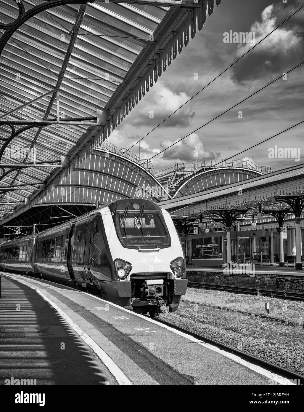 A train stands at a historic platform of a railway station. Two arches ...