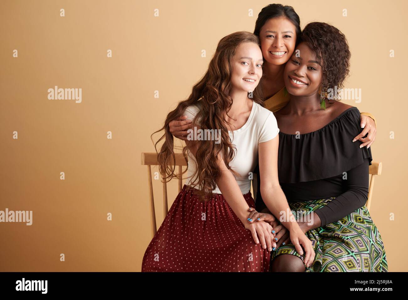 Smiling young Vietnamese woman hugging her friends sitting on chairs in ...