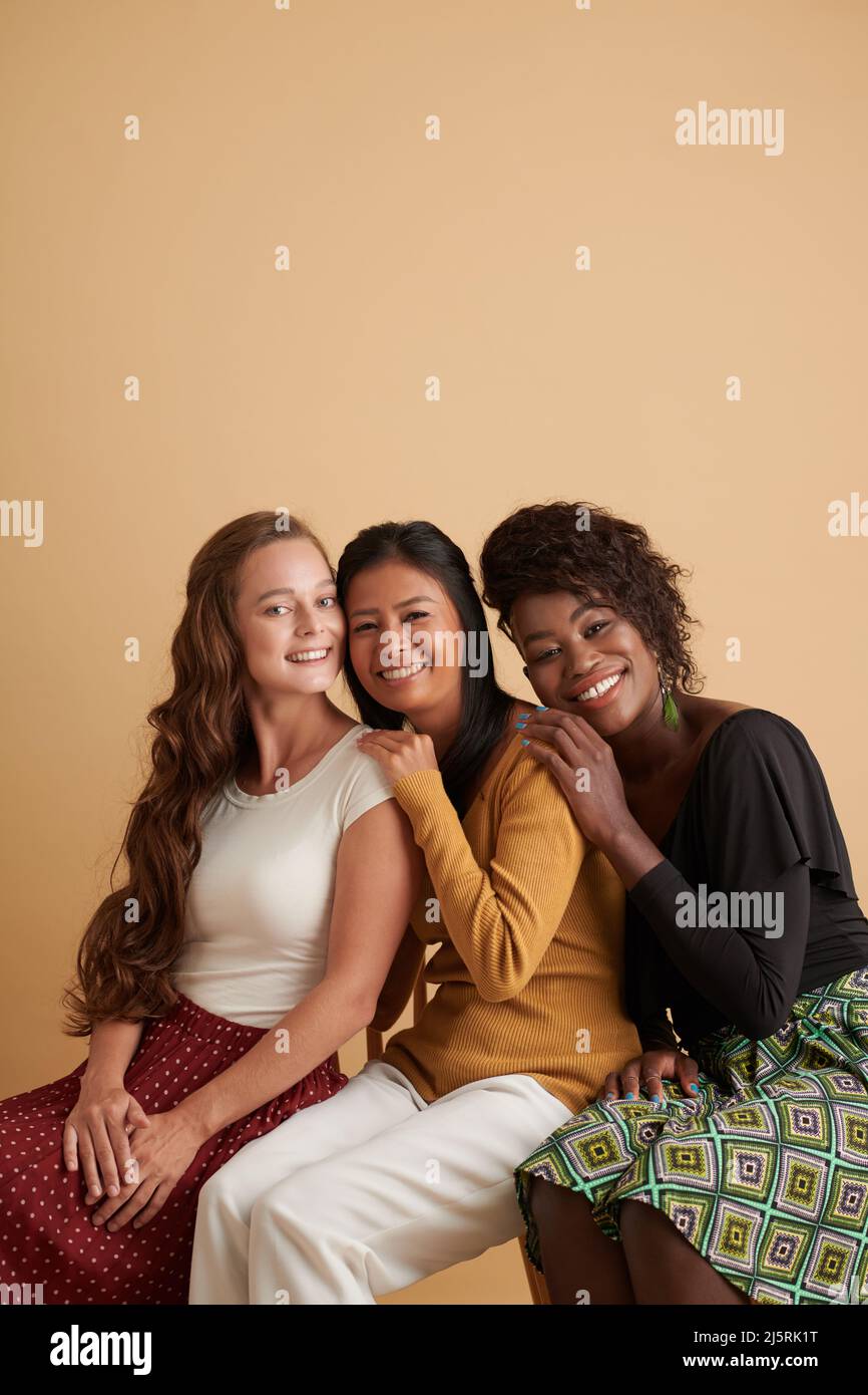 Studio portrait of happy young female friends leaning on each other ...