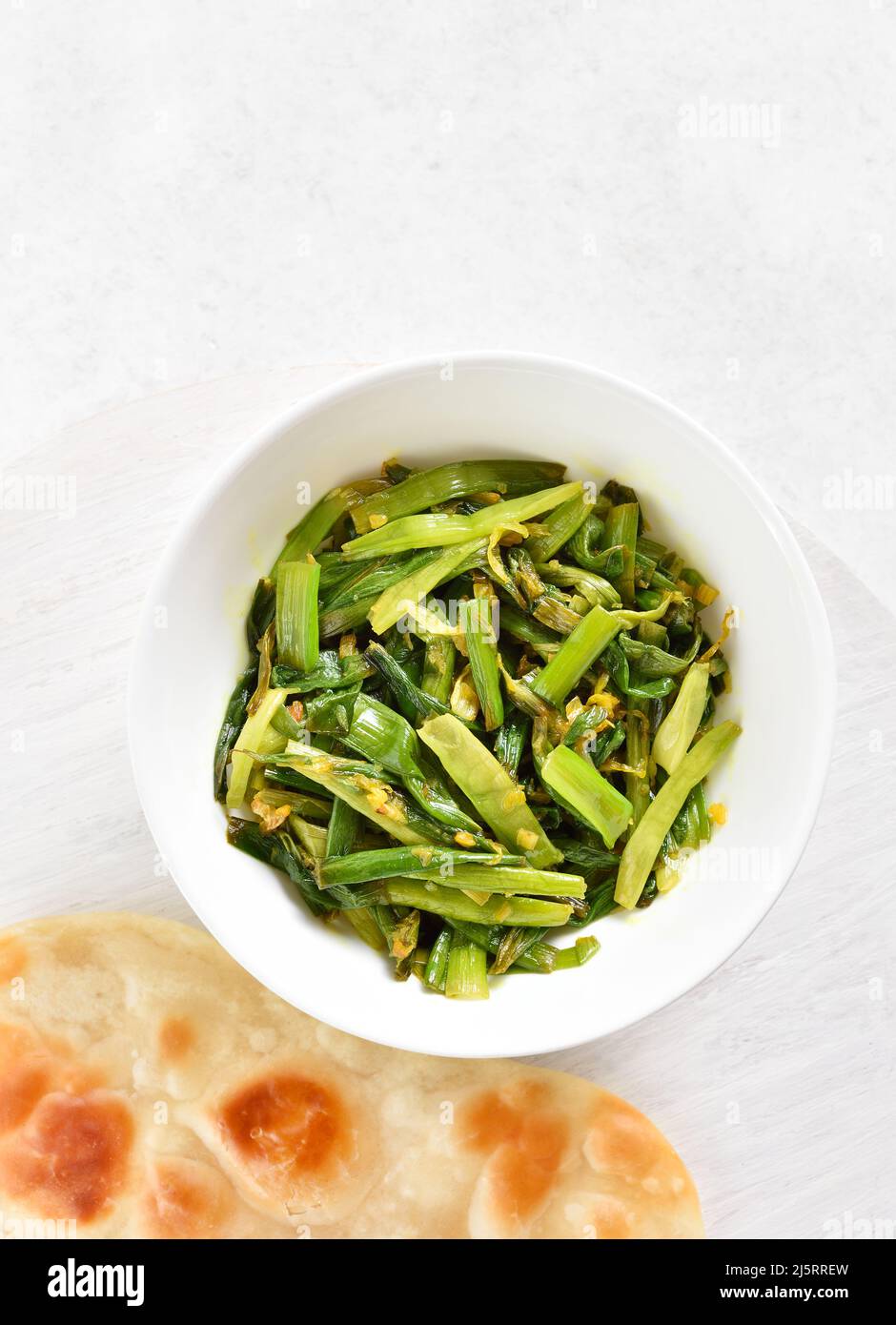 Indian style spring onion stir fry in bowl over white background with ...