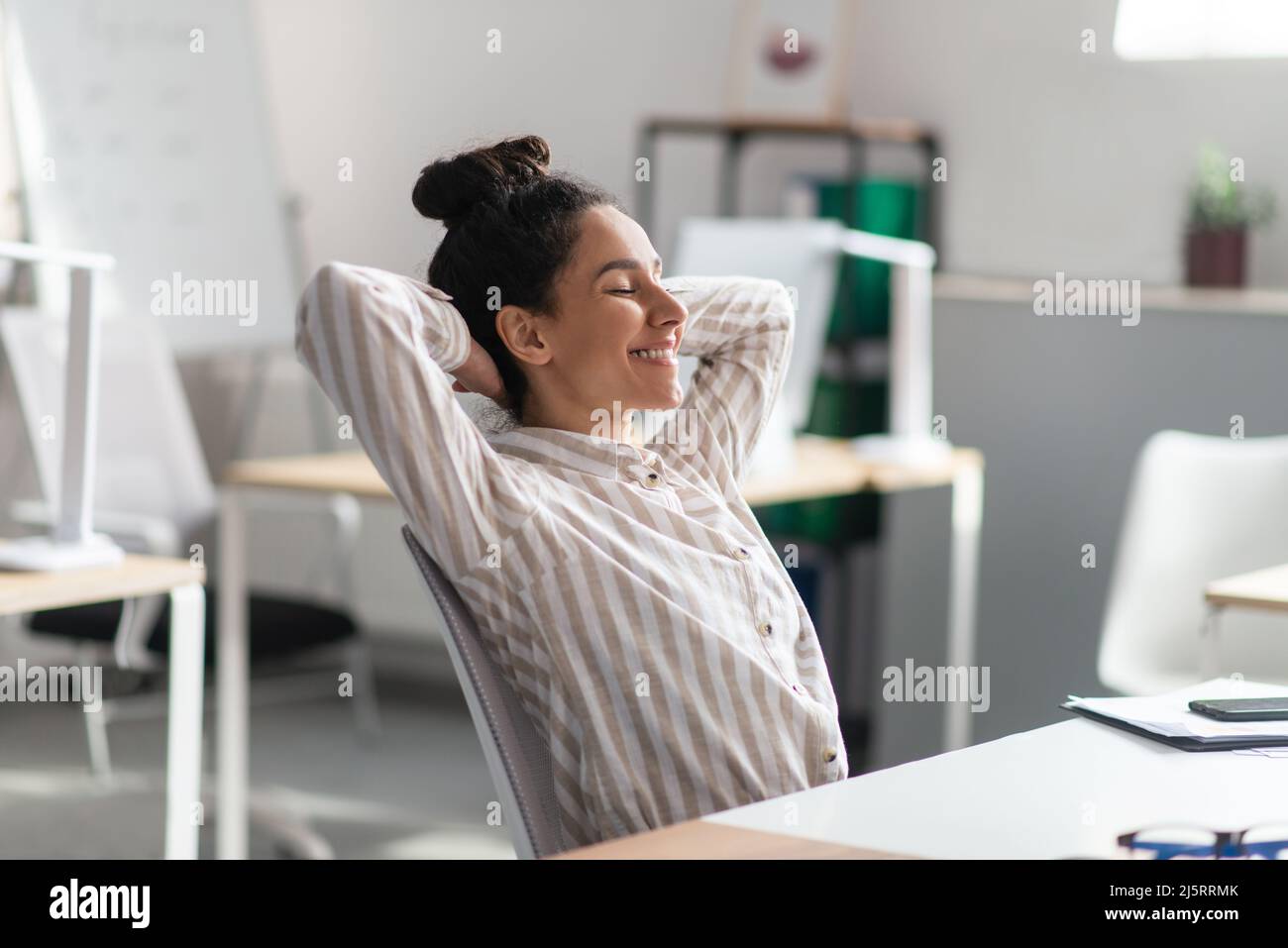 Calm female company employee leaning on chair with hands behind head ...