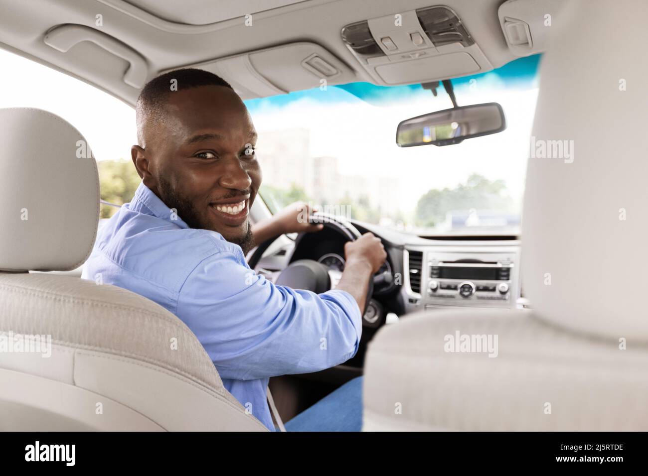 Smiling black man driving new car in city turning back Stock Photo - Alamy