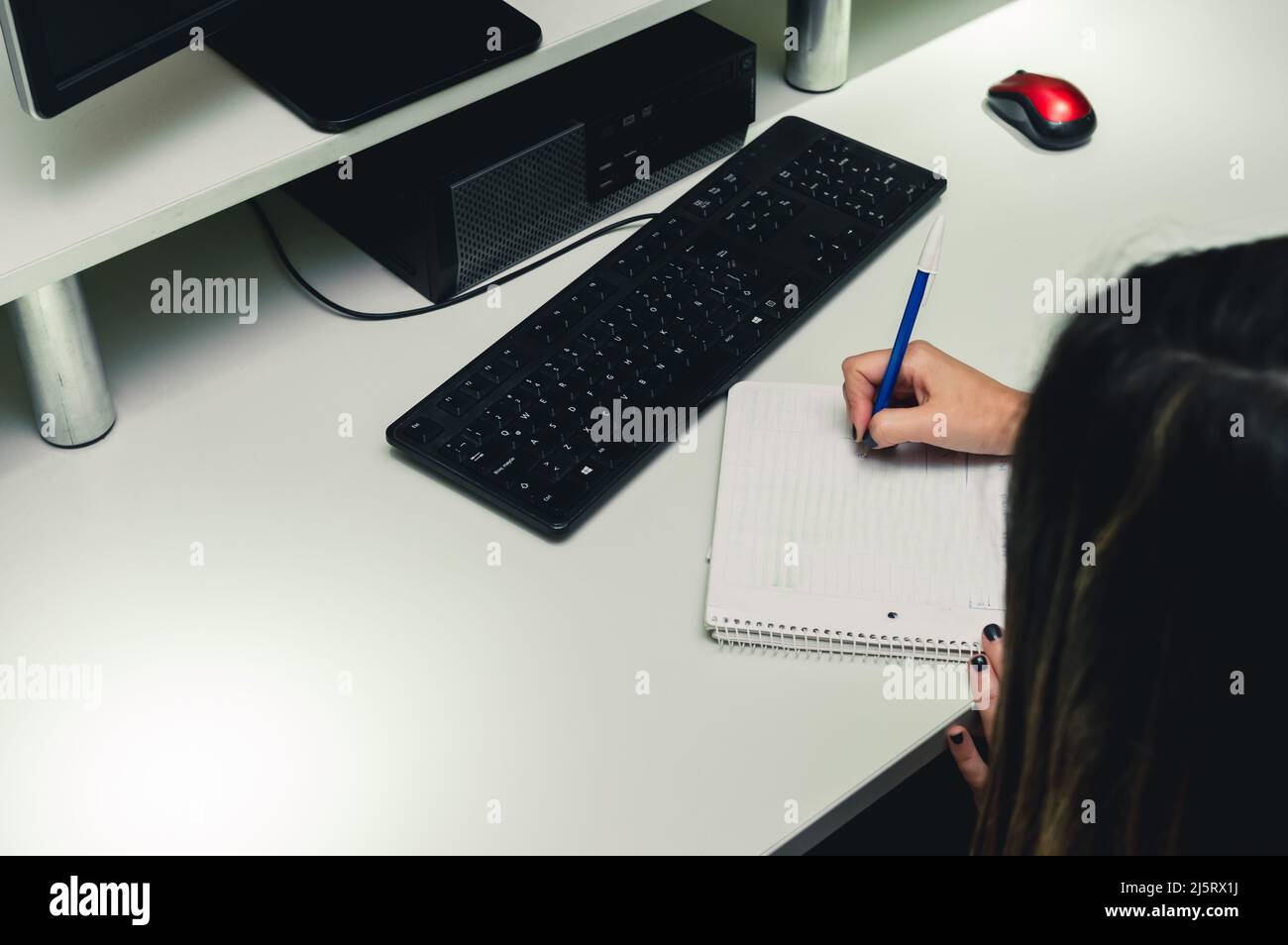 unrecognizable young woman sitting in her office writing in pad, with ...