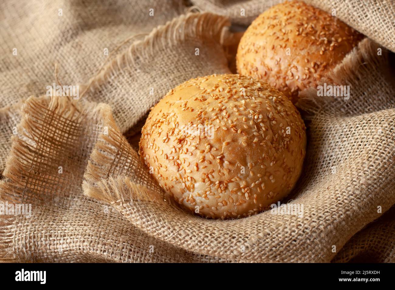 two appetizing freshly baked sesame buns are located on a coarse fabric ...