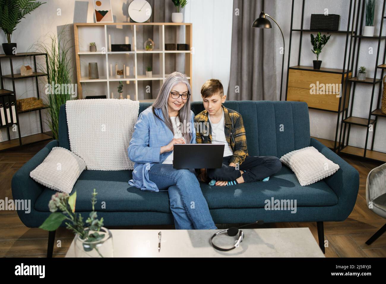 Caucasian young handsome boy teaching his old gray-haired grandmother ...