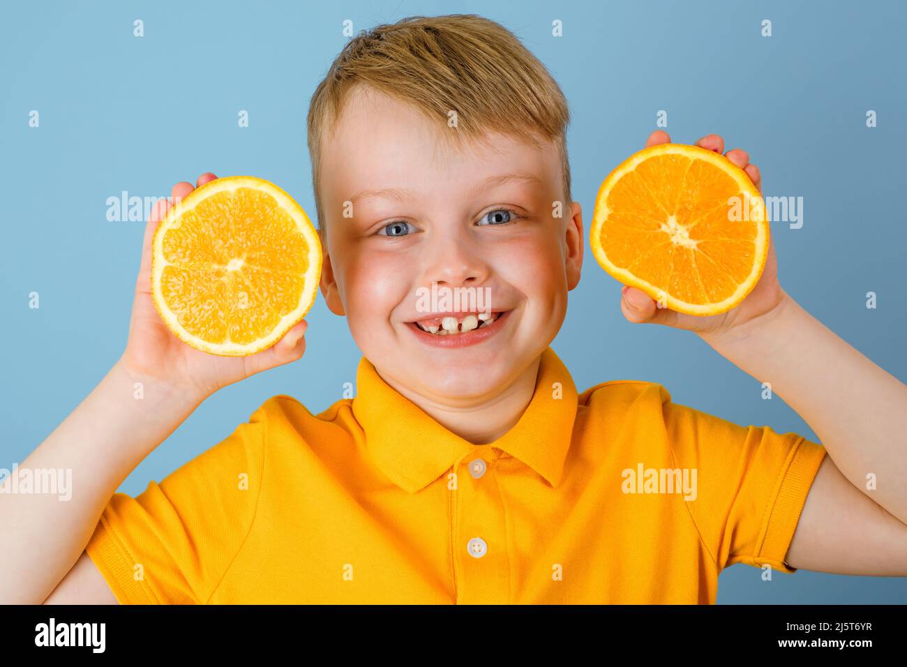 Portrait cheerful child holding two halves of a orange with his hands ...