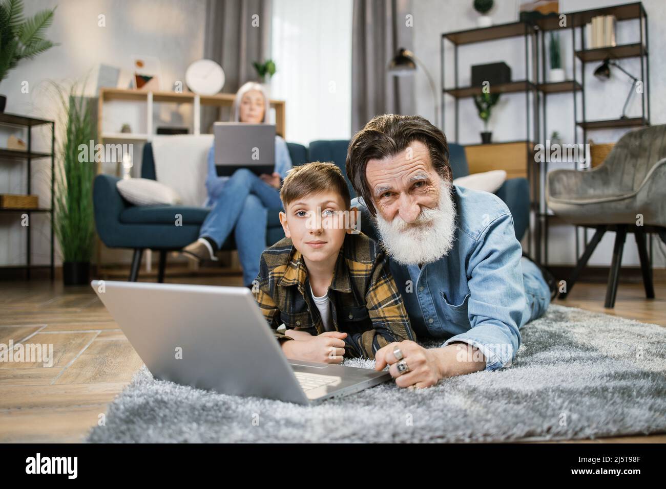Charming schoolboy playing with grandfather using laptop lying on warm ...