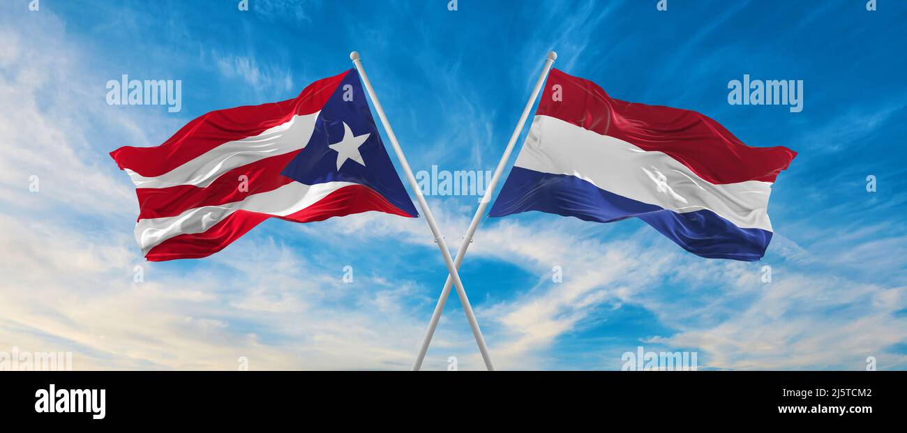 two crossed flags Puerto Rico and Netherland waving in wind at cloudy sky. Concept of ...