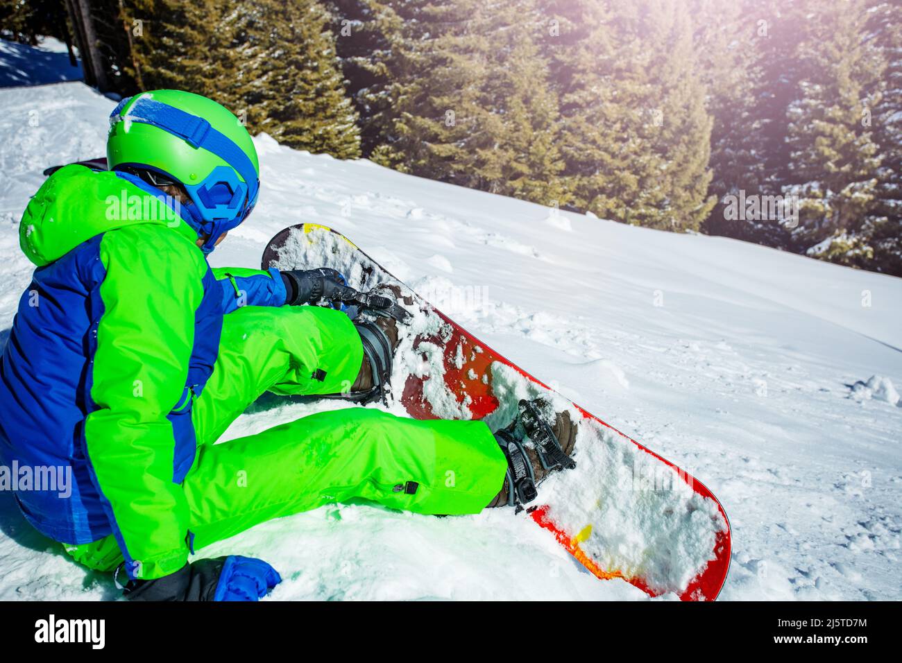 Young boy attaching snowboard sitting in the snow Stock Photo - Alamy