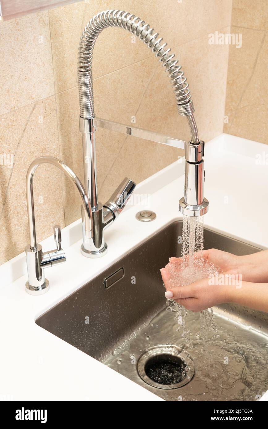 girl collects water in the palm of her hand from the tap in the kitchen ...