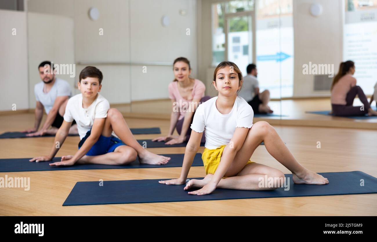 Tween girl doing twisting asana Matsyendrasana during family yoga class ...