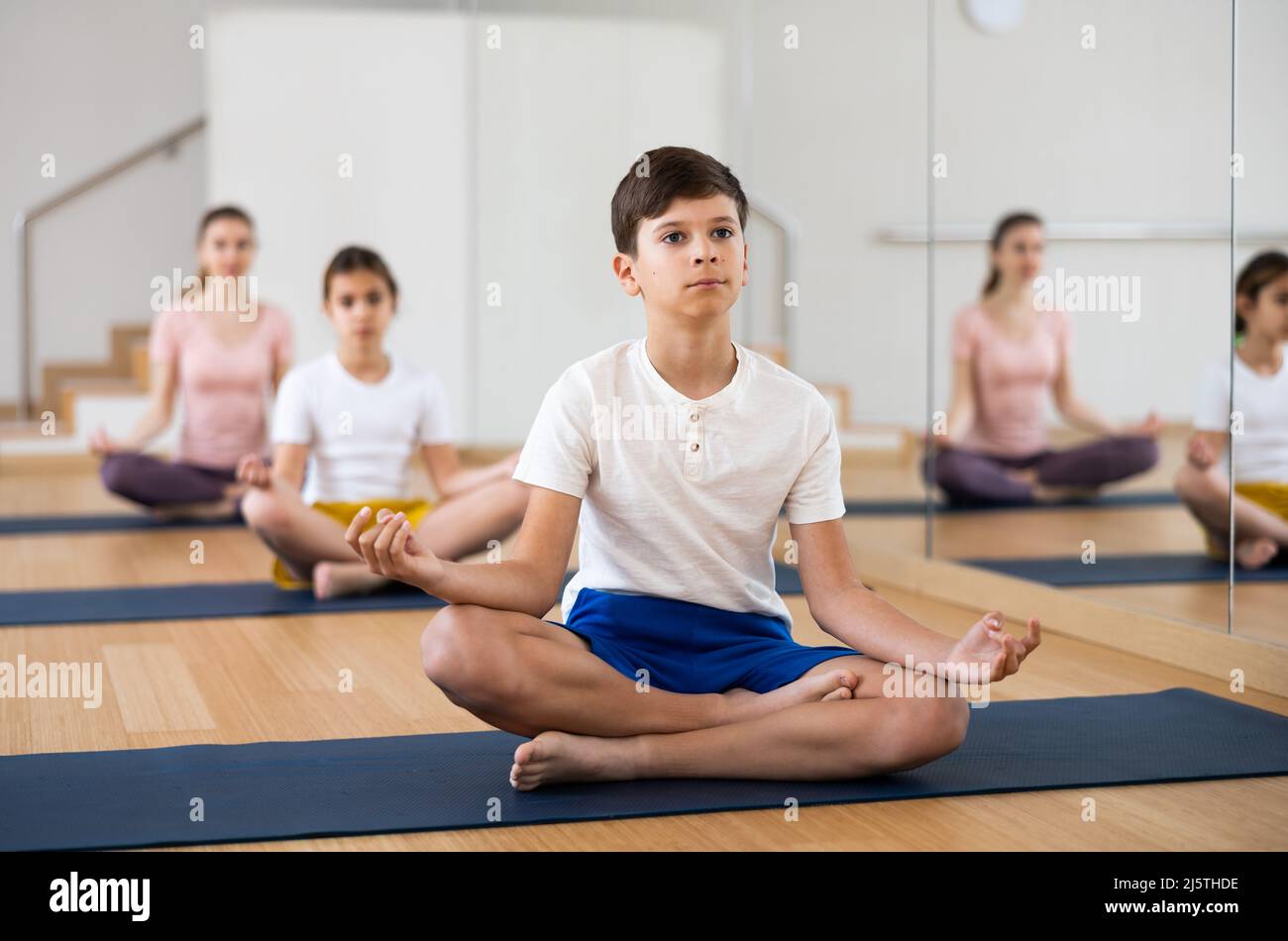 Boy sitting in lotus pose while exercising yoga with family in fitness ...