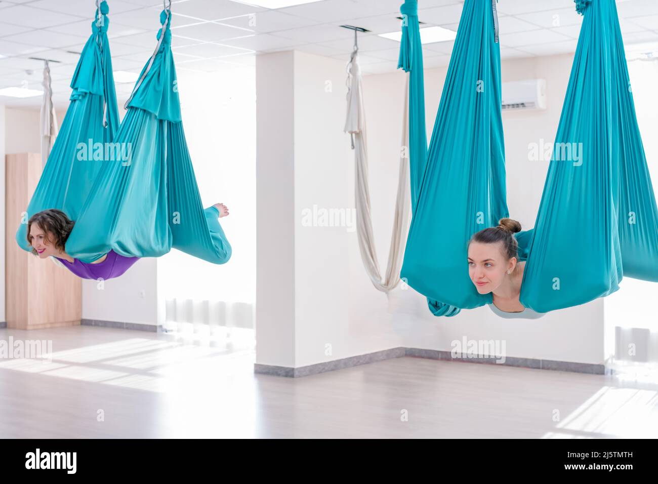 Two yogi women makes tandem yoga pose using blue hammock for fly yoga ...