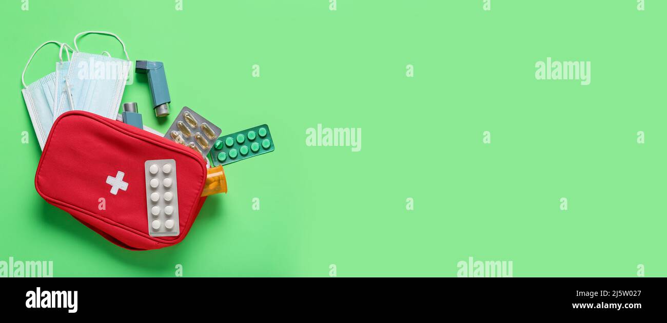 First aid kit with pills, inhalers and medical masks on green ...