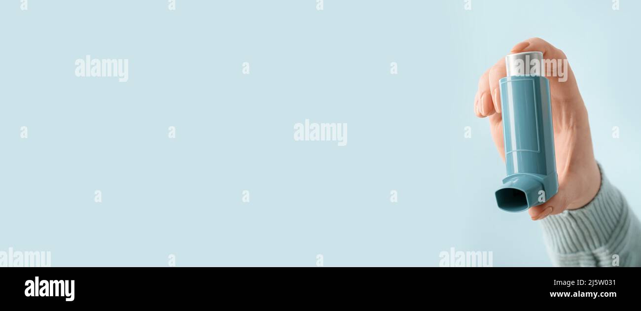 Female hand holding asthma inhaler on light blue background with space ...