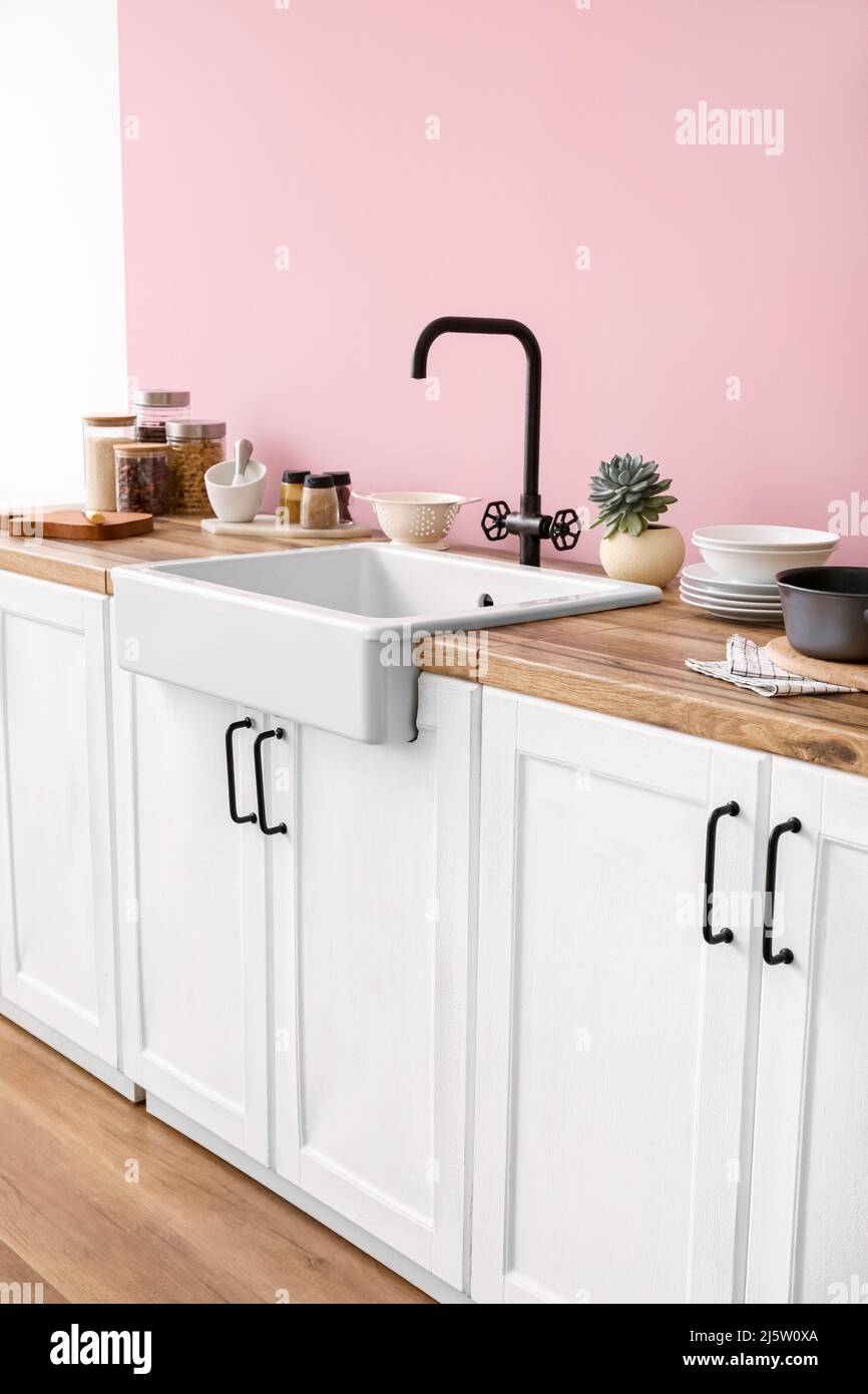 Counters with ceramic sink and kitchen utensils near pink wall Stock ...