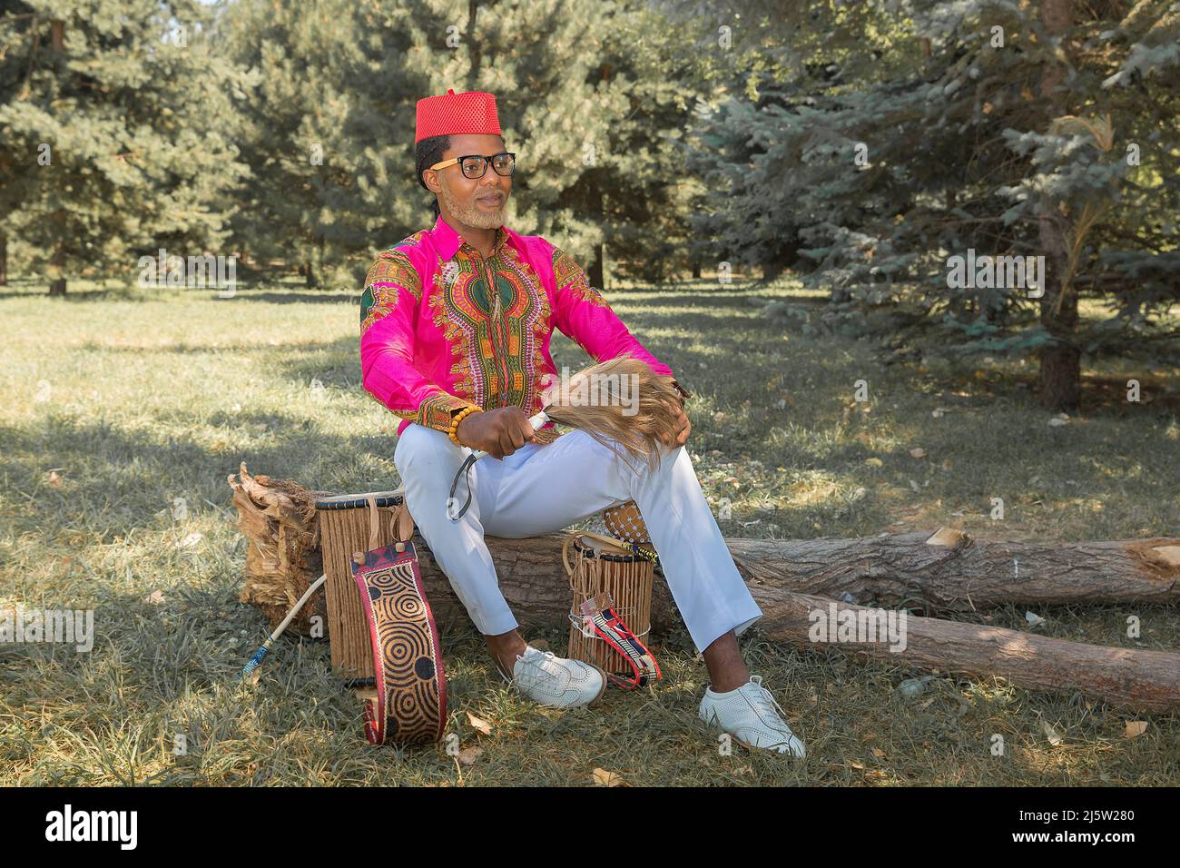 Handsome African man in a national costume plays an ethnic drum, djembe ...
