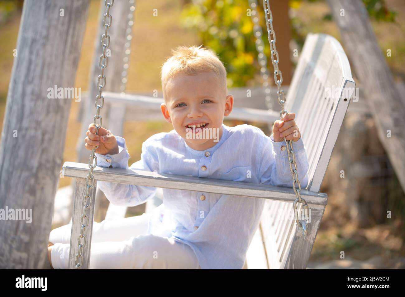 Happy child boy laughing and swinging on a swing at summer garden. Spring kids portrait. Kid ...